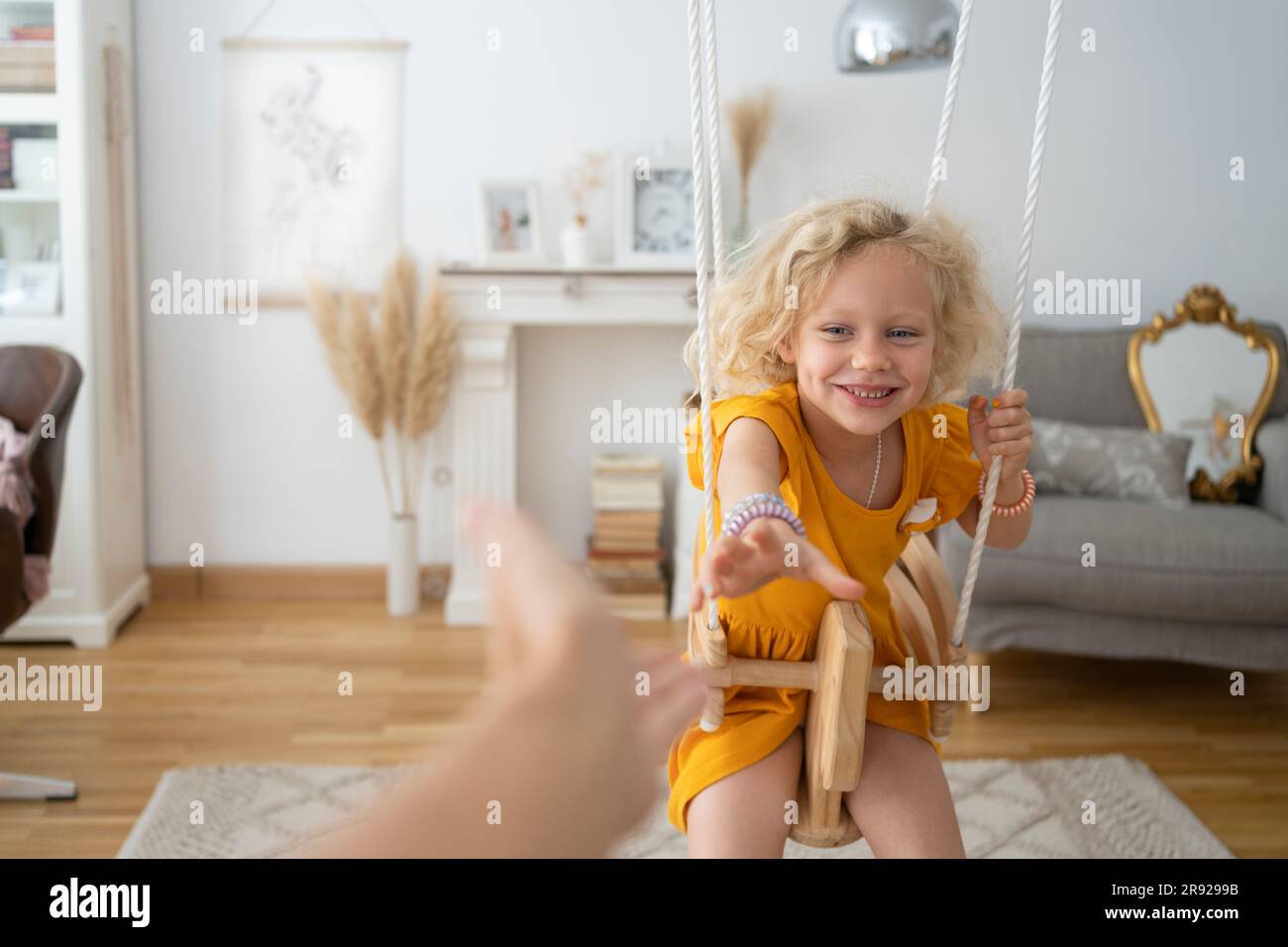 Happy girl swinging and reaching mother's hand at home Stock Photo - Alamy
