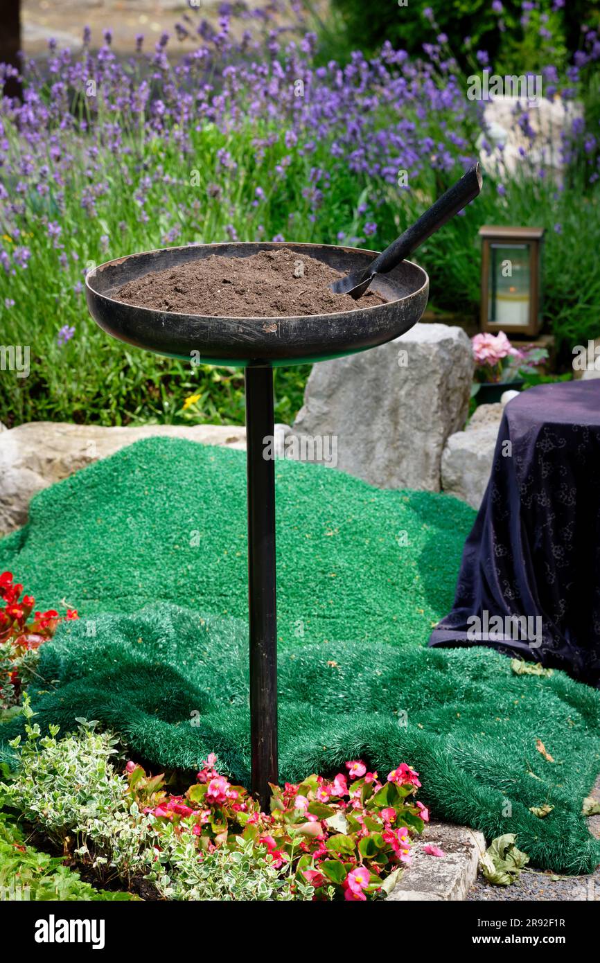 an urn grave prepared for burial with green grass mats and a bowl of ...