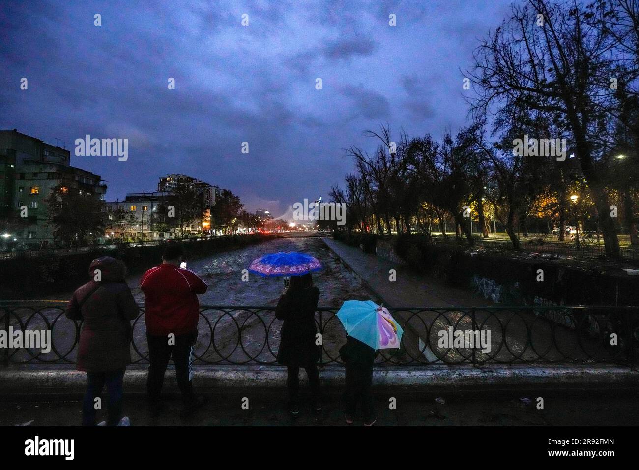 People watch the water level of the Mapocho River rise during a heavy ...