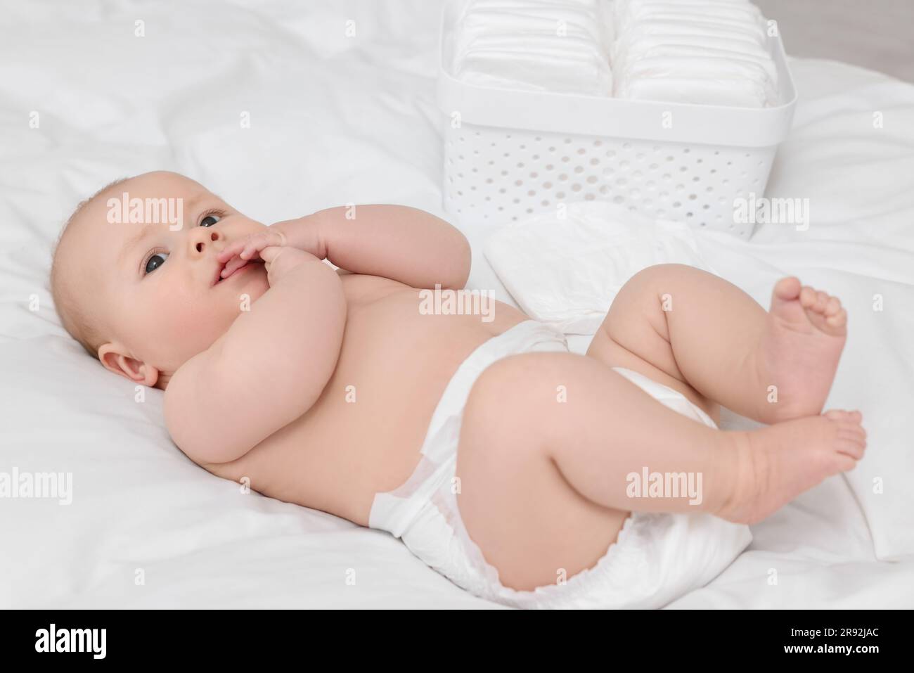 Cute baby and diapers on white bed Stock Photo - Alamy