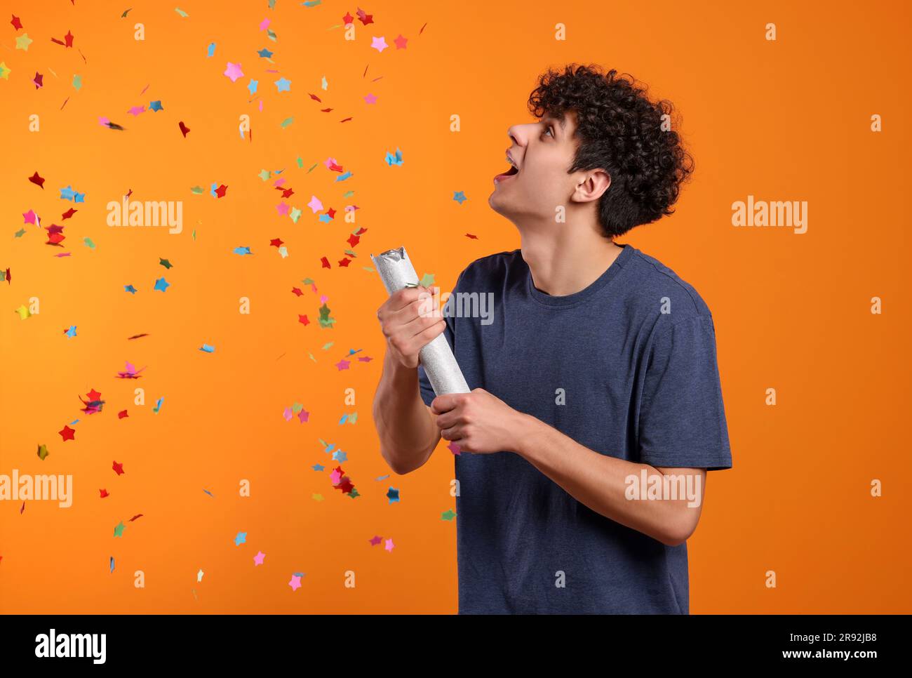 Emotional young man blowing up party popper on orange background Stock ...