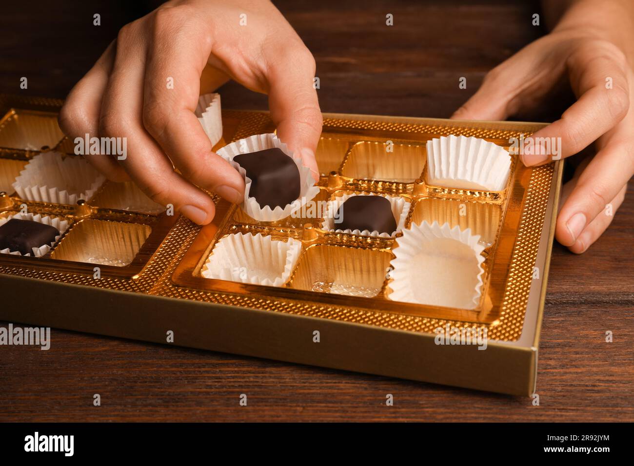 Woman taking chocolate candy out from box at wooden table, closeup ...