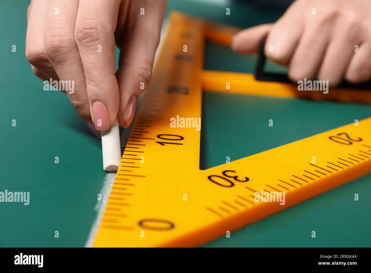 Woman drawing with chalk and triangle ruler on green board, closeup ...