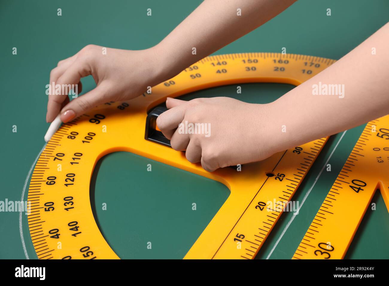 Woman drawing with chalk, triangle ruler and protractor on green board ...