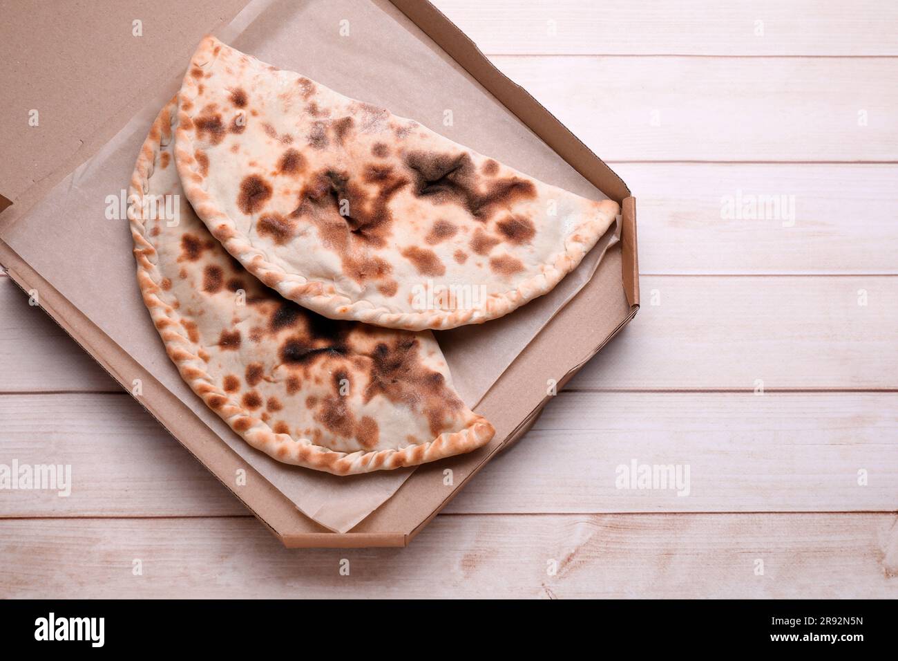 Cardboard box with delicious calzones on light wooden table, top view ...
