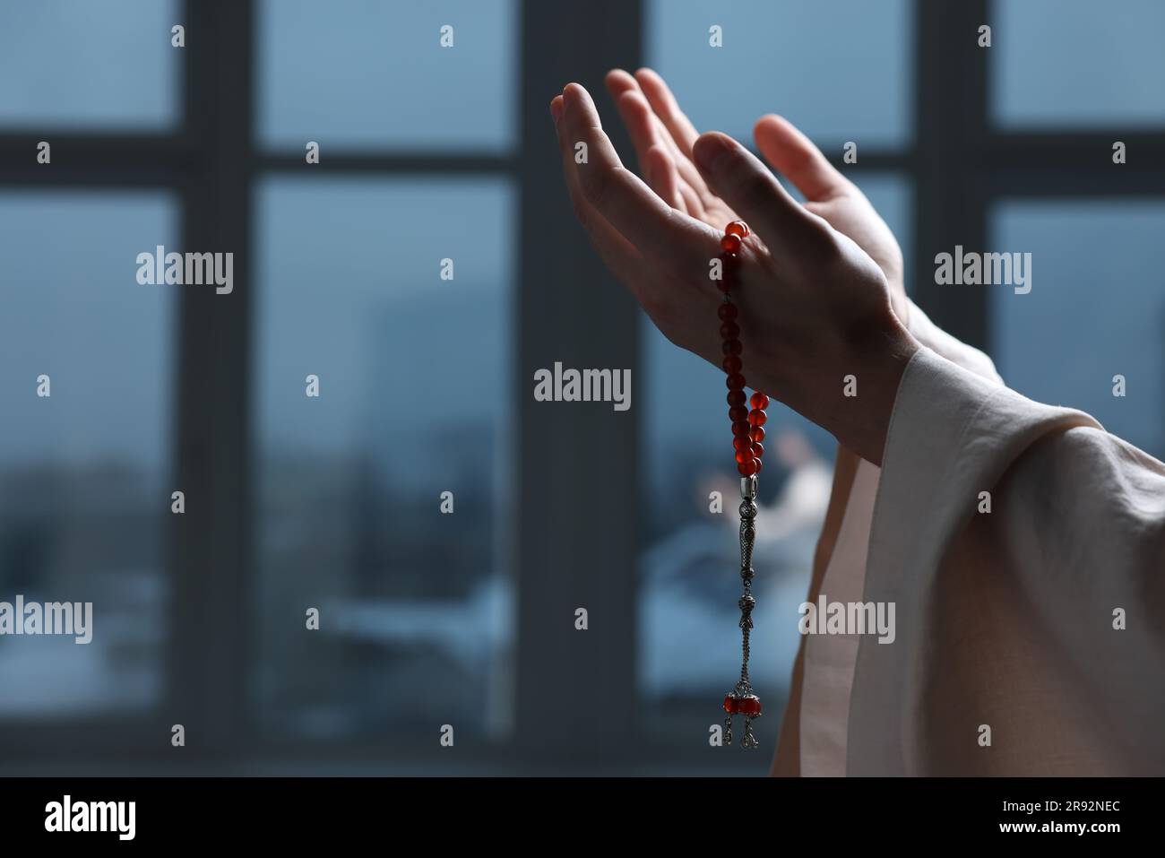 Muslim man with misbaha praying near window indoors, closeup. Space for ...