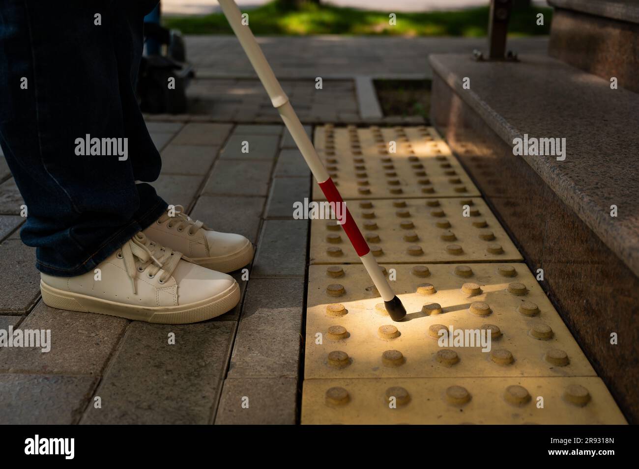 A close-up of a woman's feet with a tactile cane and a tactile tile ...