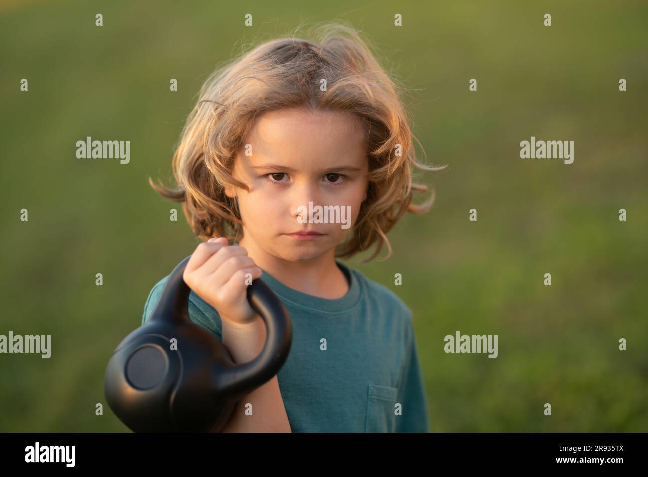 Child lifting the kettlebell in park outside. Child workout. Kid sport ...