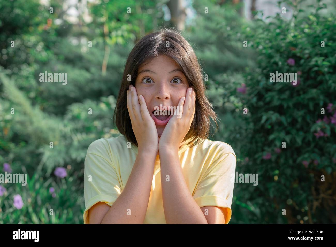 Frightened young girl with wide open eyes. The girl covered her face with her hands, while ...