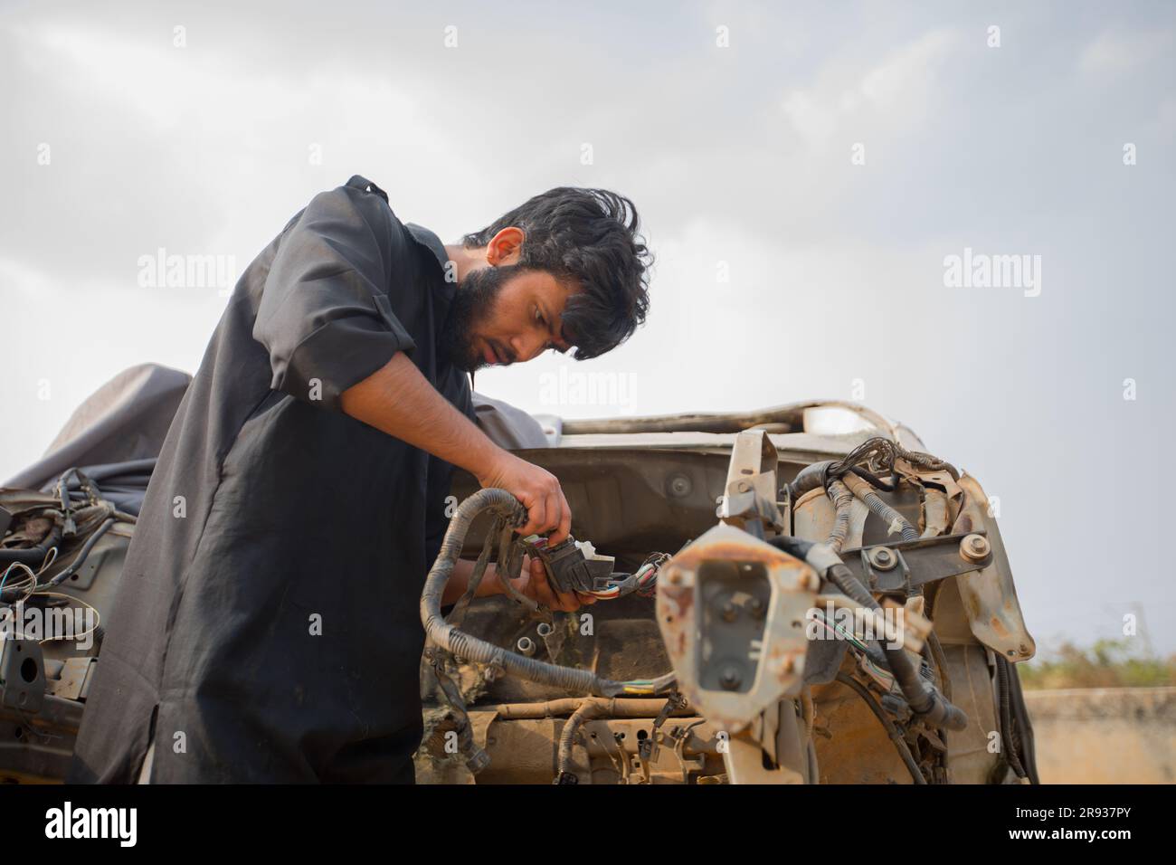 A mechanical worker repairing an old and damaged vehicle in an open ...