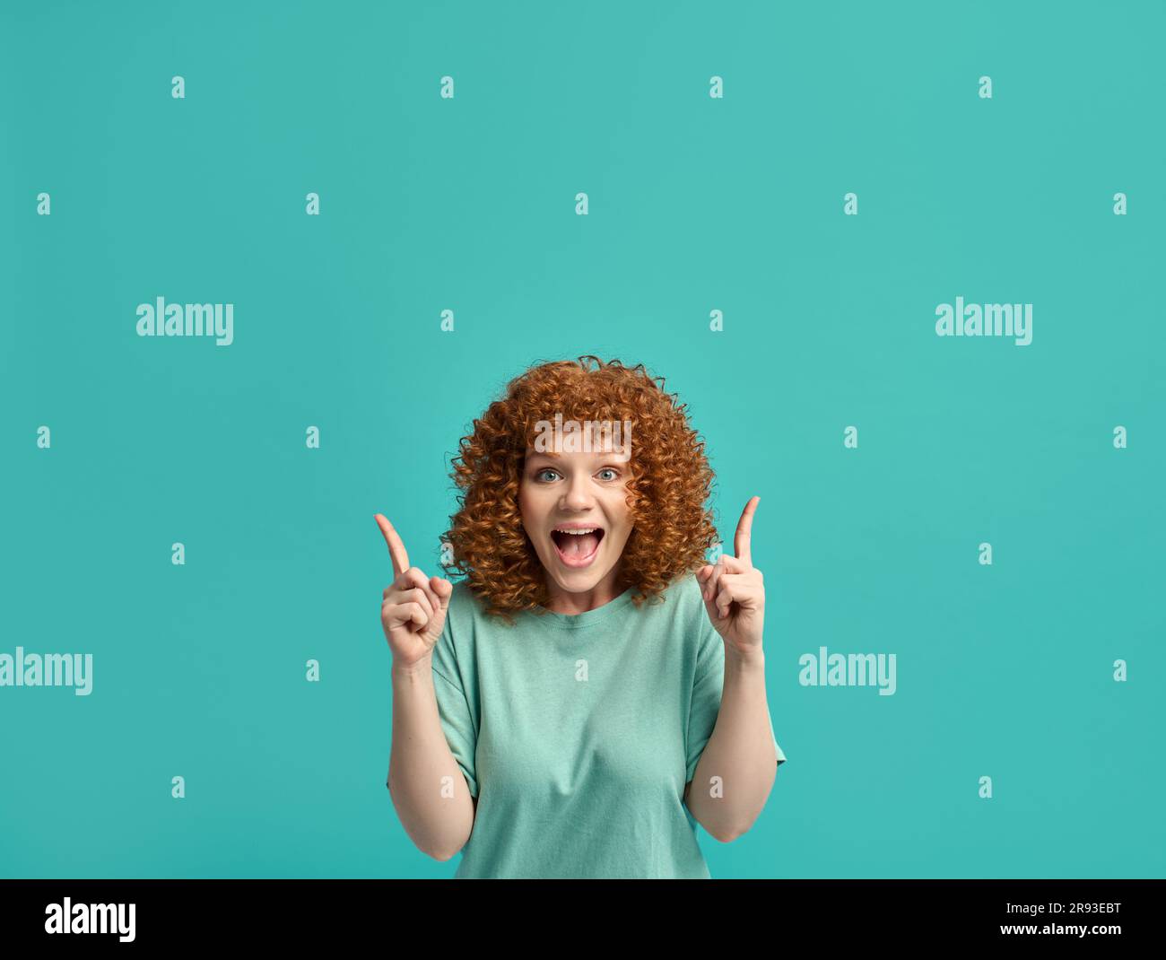 Excited young ginger teenager girl smiling and pointing index fingers ...