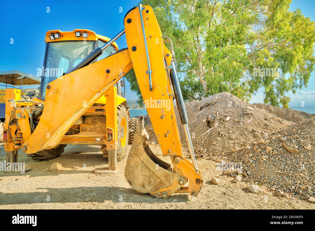 Side view of yellow excavator with long arm along coastal road. Work in ...