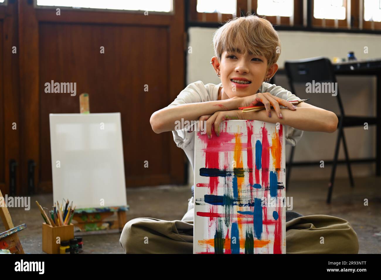 Portrait of young female student sitting in art workshop, holding ...
