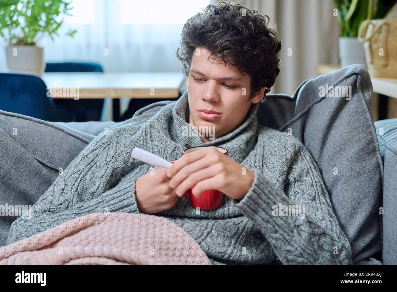Young guy checking temperature, lying on couch under blanket Stock ...