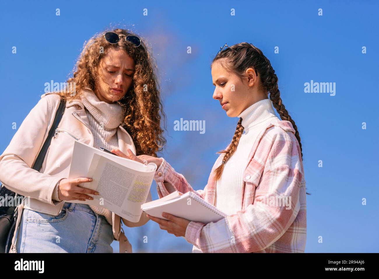 Two beautiful high school girls reading a book together and discussing ...