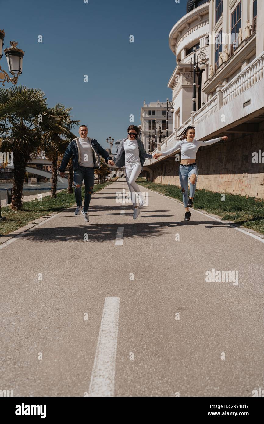 Three friends laughing while jumping and holding hands at the beautiful ...