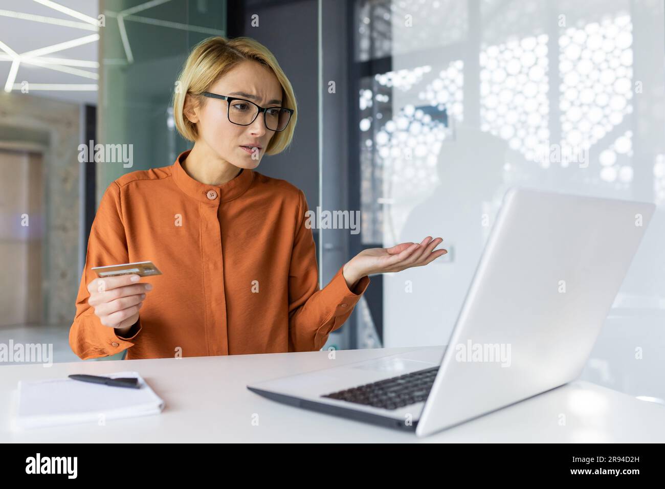 Sad and unhappy woman inside workplace office with laptop holding bank ...