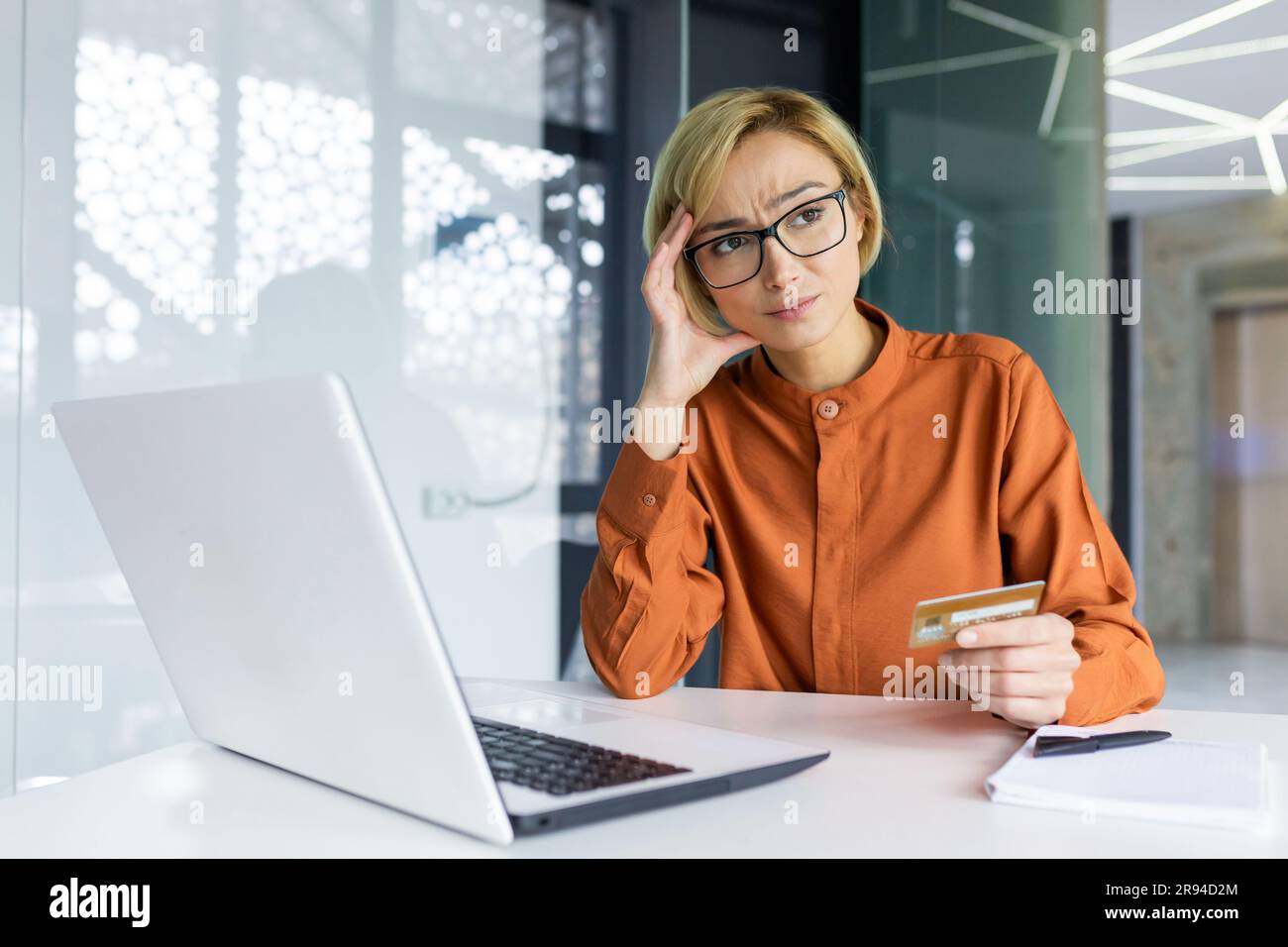 Sad and unhappy woman inside workplace office with laptop holding bank ...