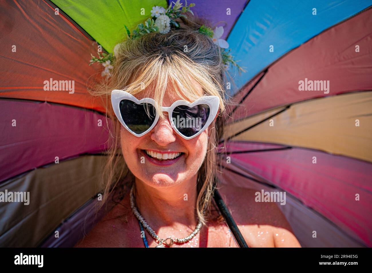 A woman wears sunglasses and uses a colourful brolly to shade from the ...