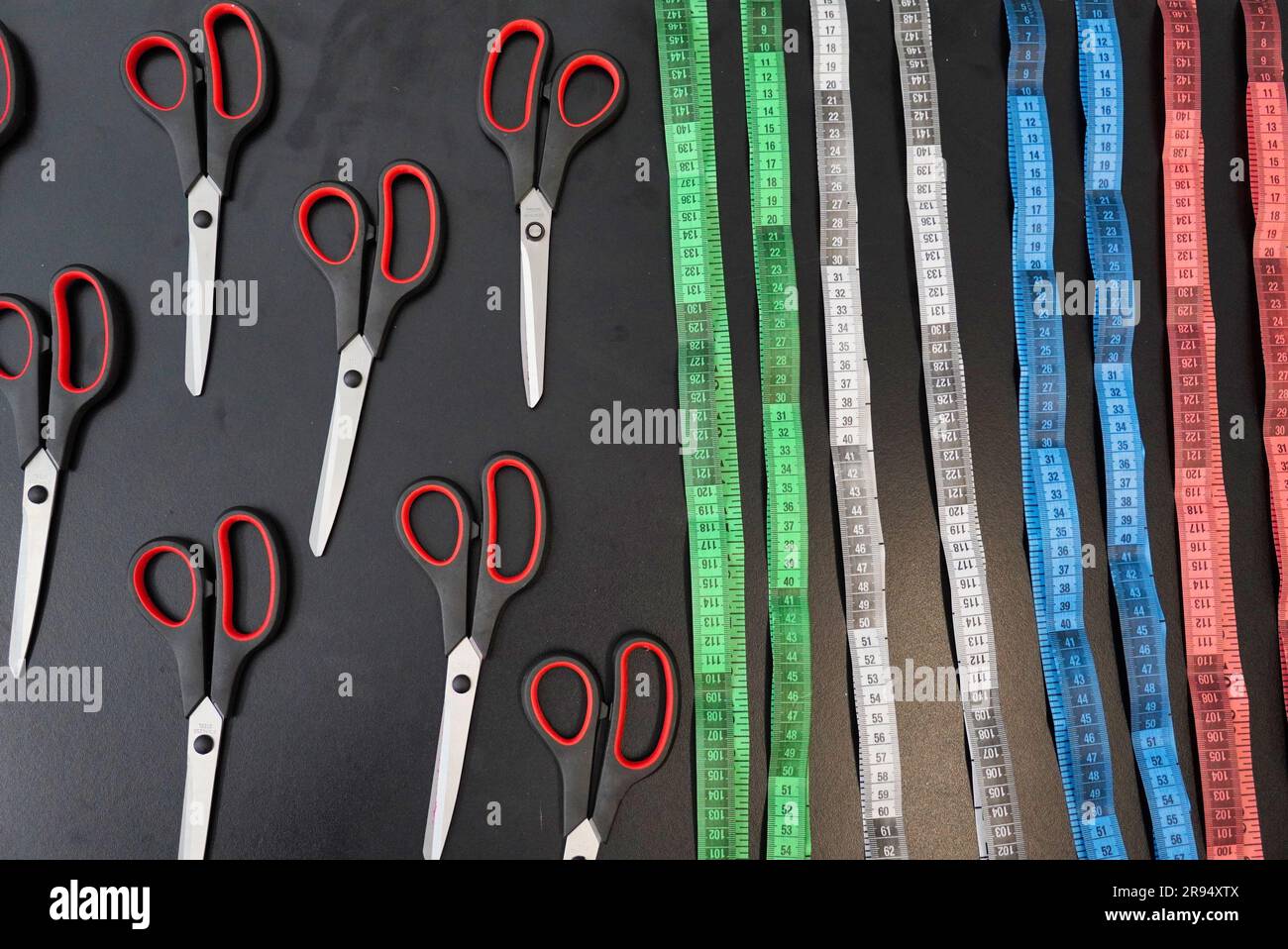 A collection of scissors and measuring tapes on the black tabletop ...