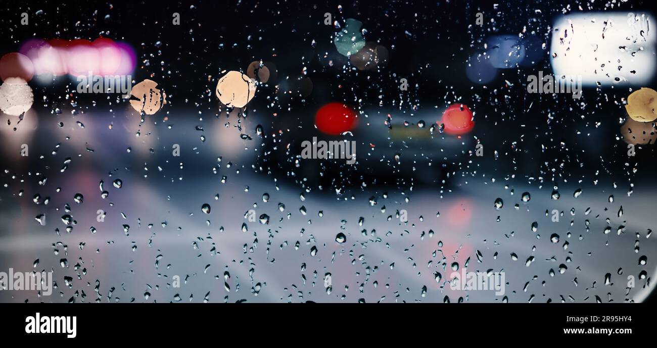 Rain shower on car windshield or car window and blurry road in background. Driving in rainy ...