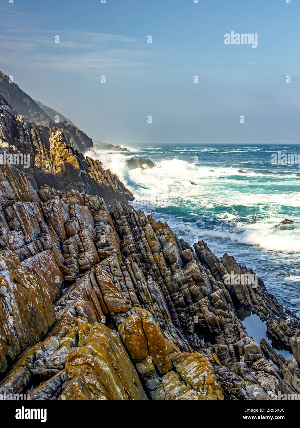 Waves breaking against the tilted rock layers aong the rocky ...