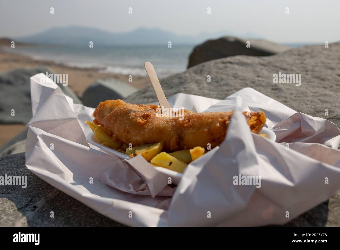 Fish and chips, battered cod, in a tray wrapped in paper with a wooden ...