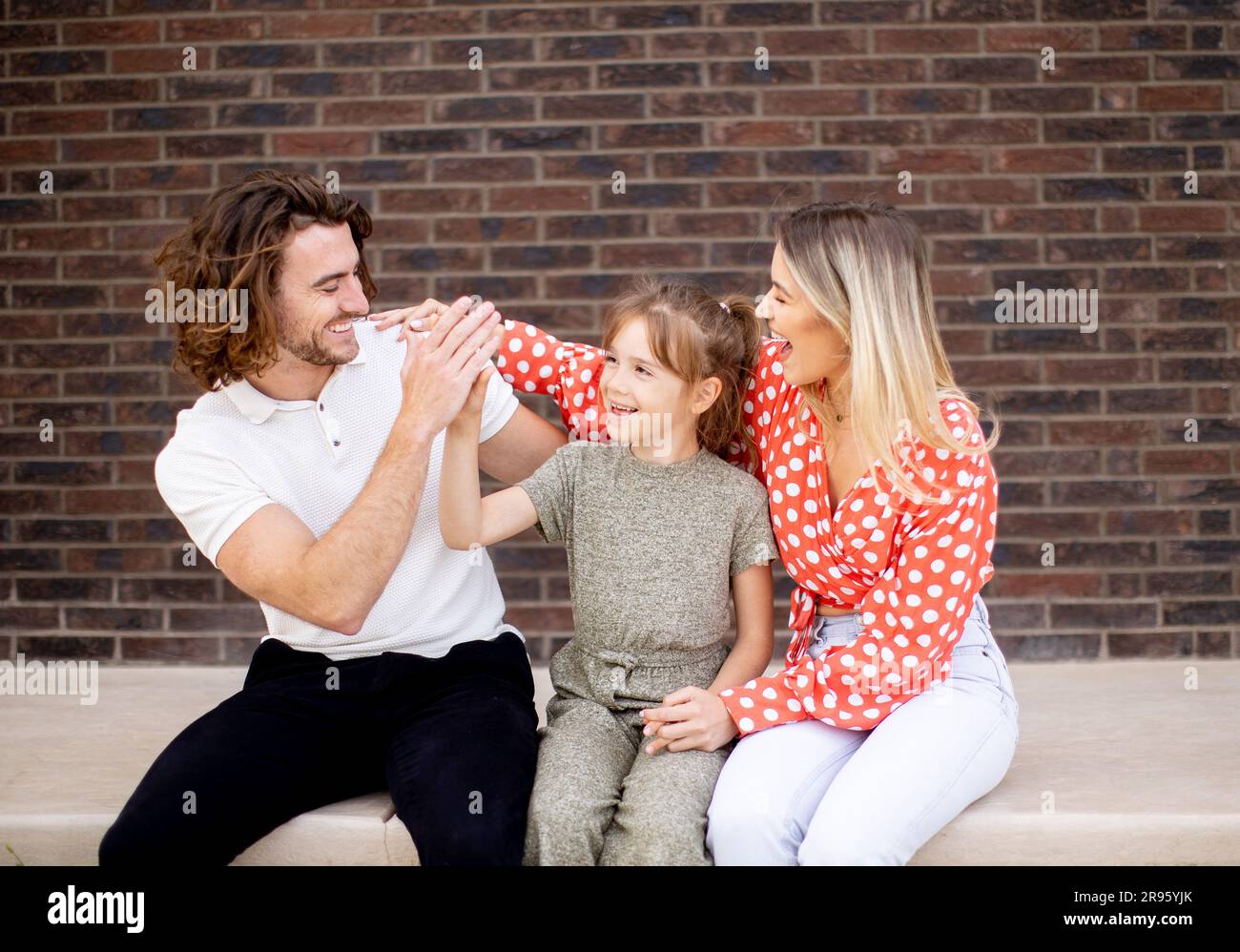 Family with a mother, father and daughter sitting outside on steps of a ...