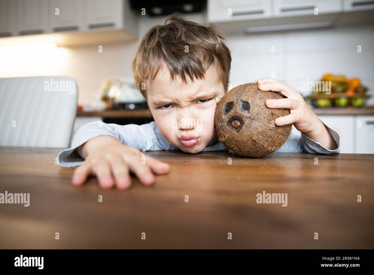 Portrait caucasian boy at table in kitchen home, depicts angry coconut ...