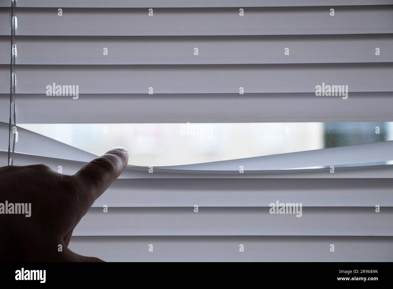 finger on the blinds on the window of the house, look out the window ...