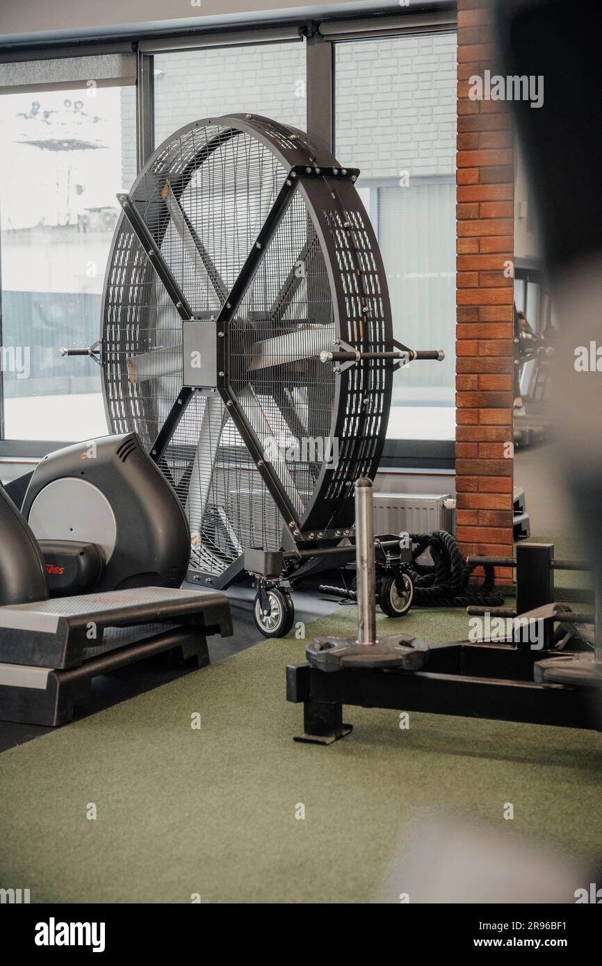 An indoor gym with two pieces of workout equipment, a large fan, and ...