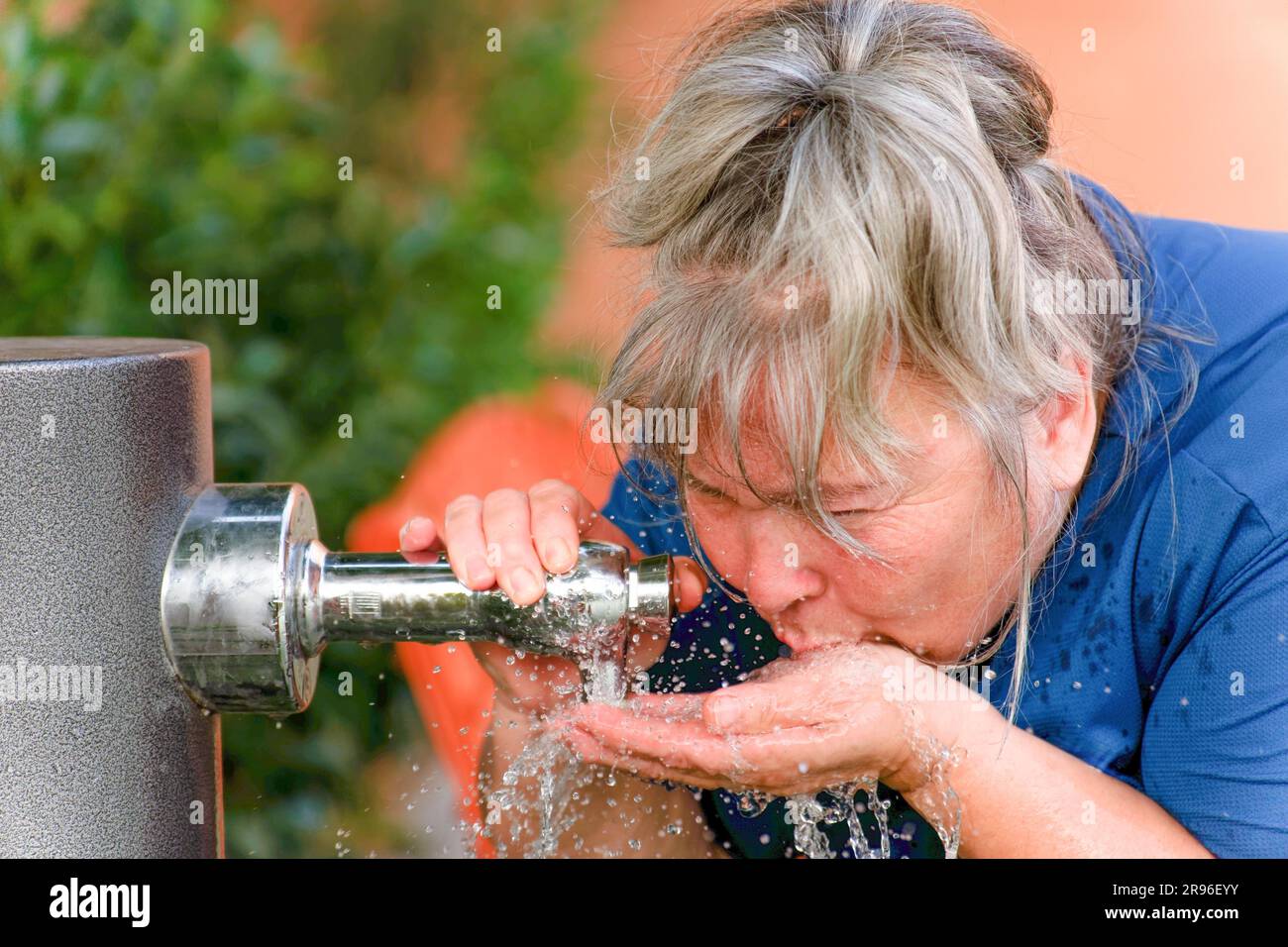 Woman with white hair drinking water from a fountain splashing in her ...