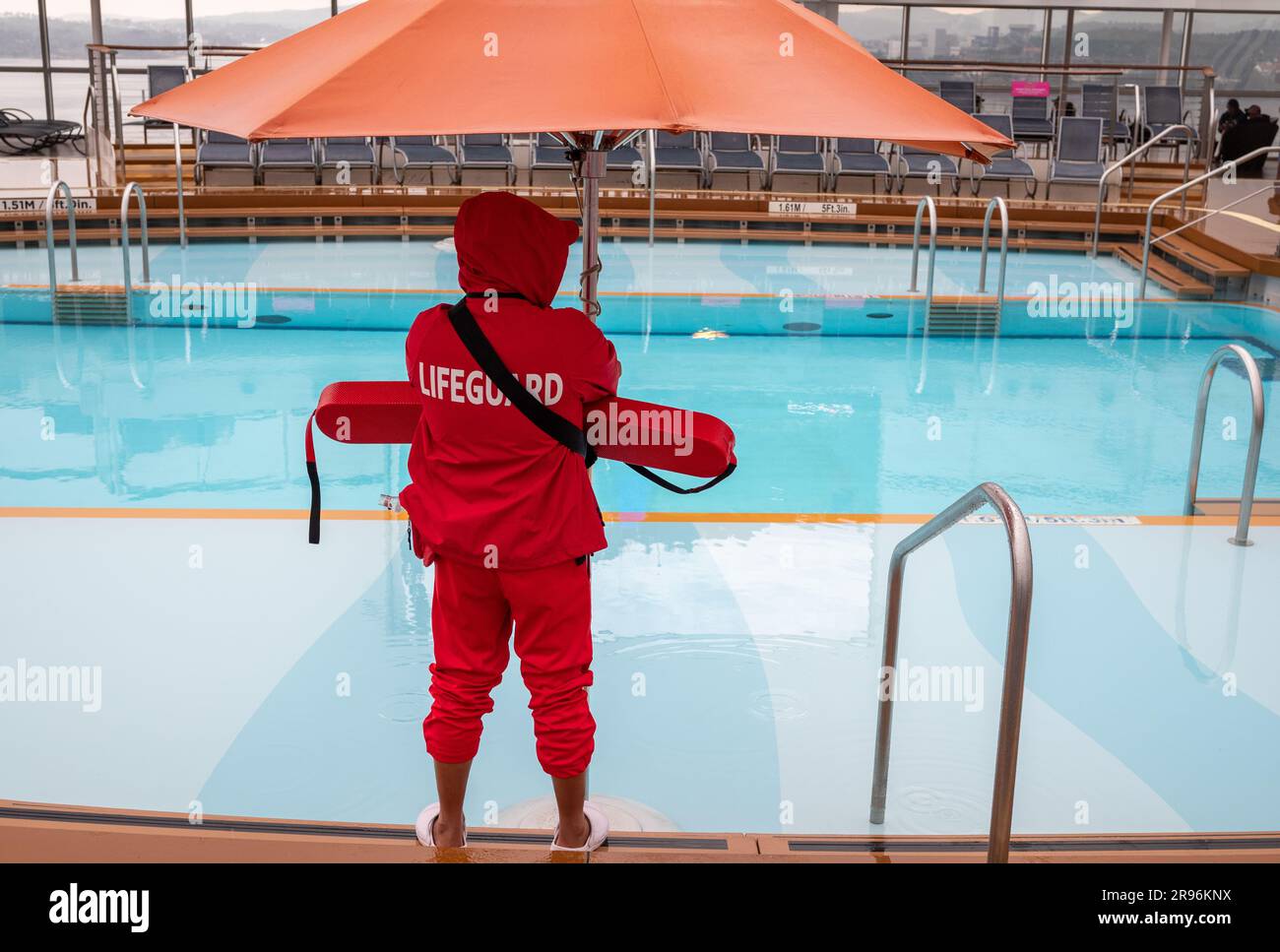 Lifeguard standing in front of an empty swimming pool on a rainy day ...