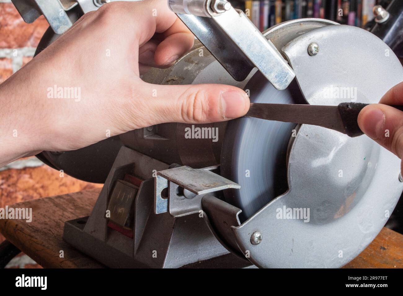 A knife sharpener and hand with a blade on a wooden table, close-up ...