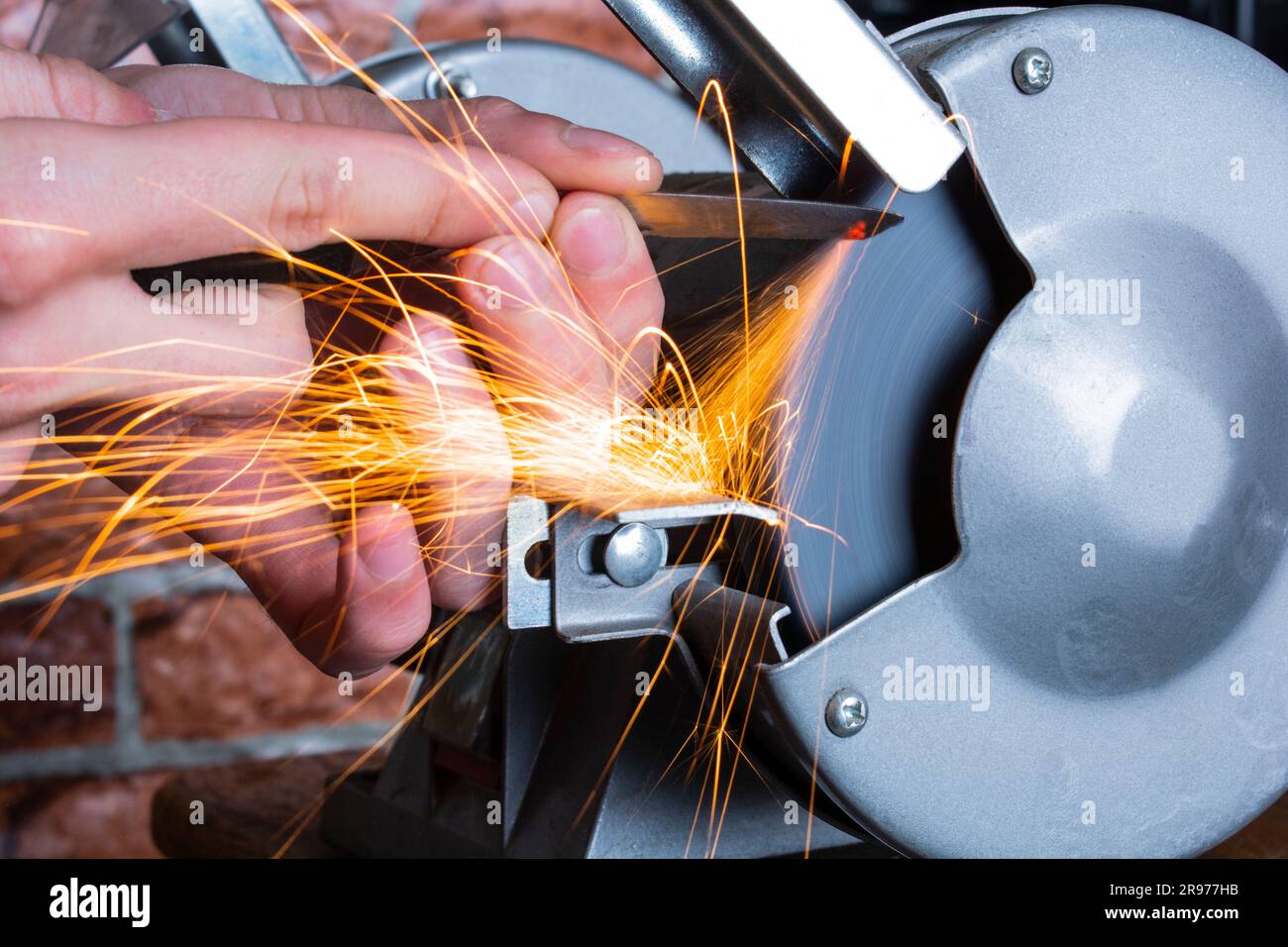 A knife sharpener and hand with a blade on a wooden table, close-up ...