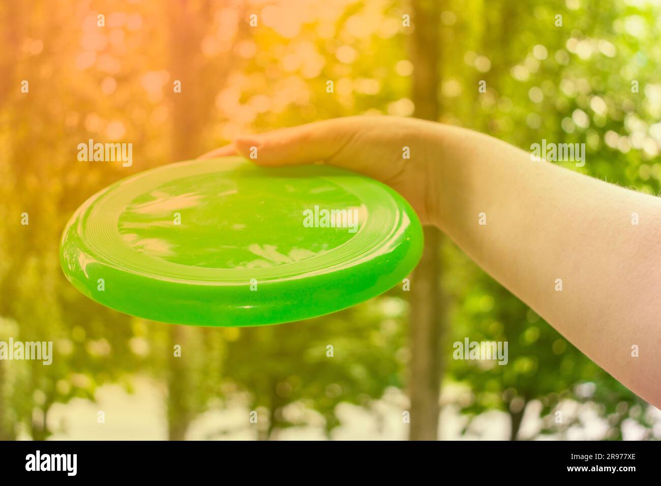 hand throwing a frisbee disc in the park on a summer day with a flash ...