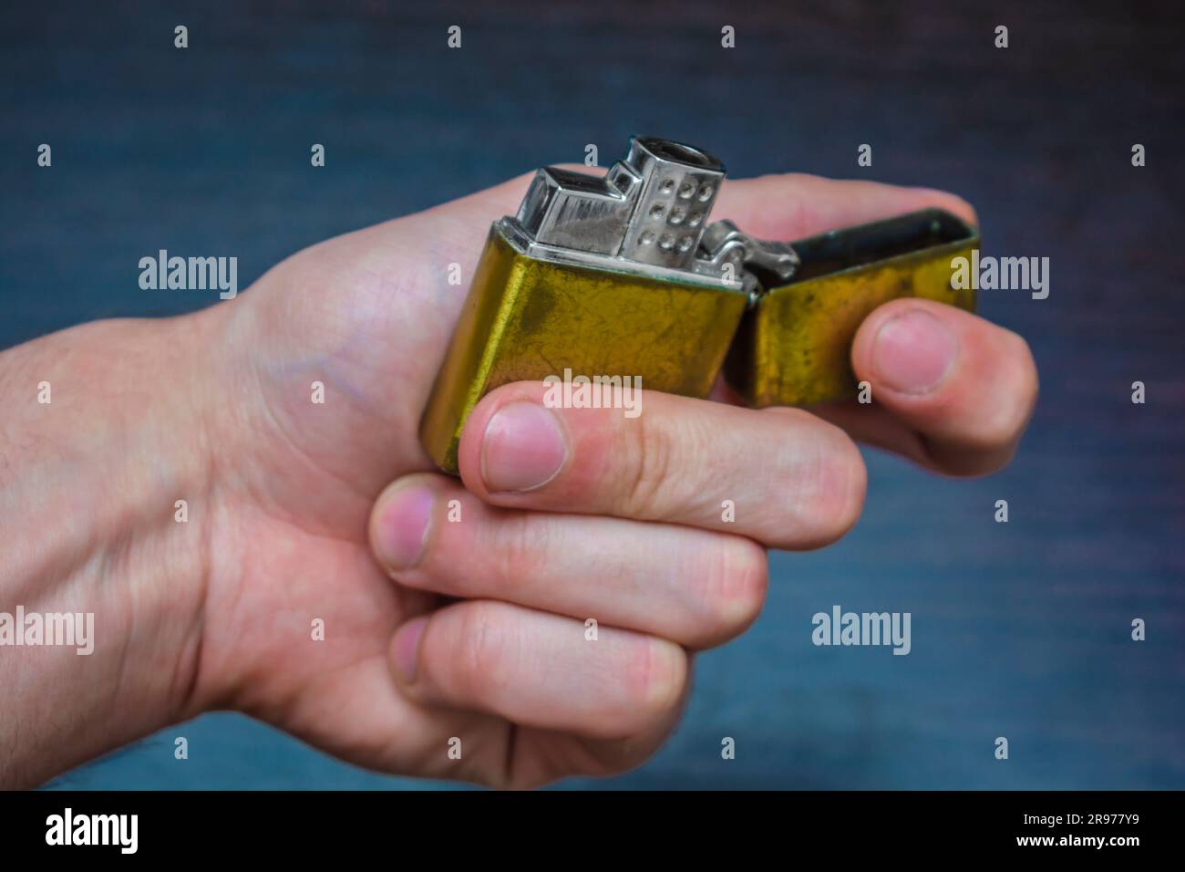 hand-held golden folding lighter on a dark background in yellow-blue ...