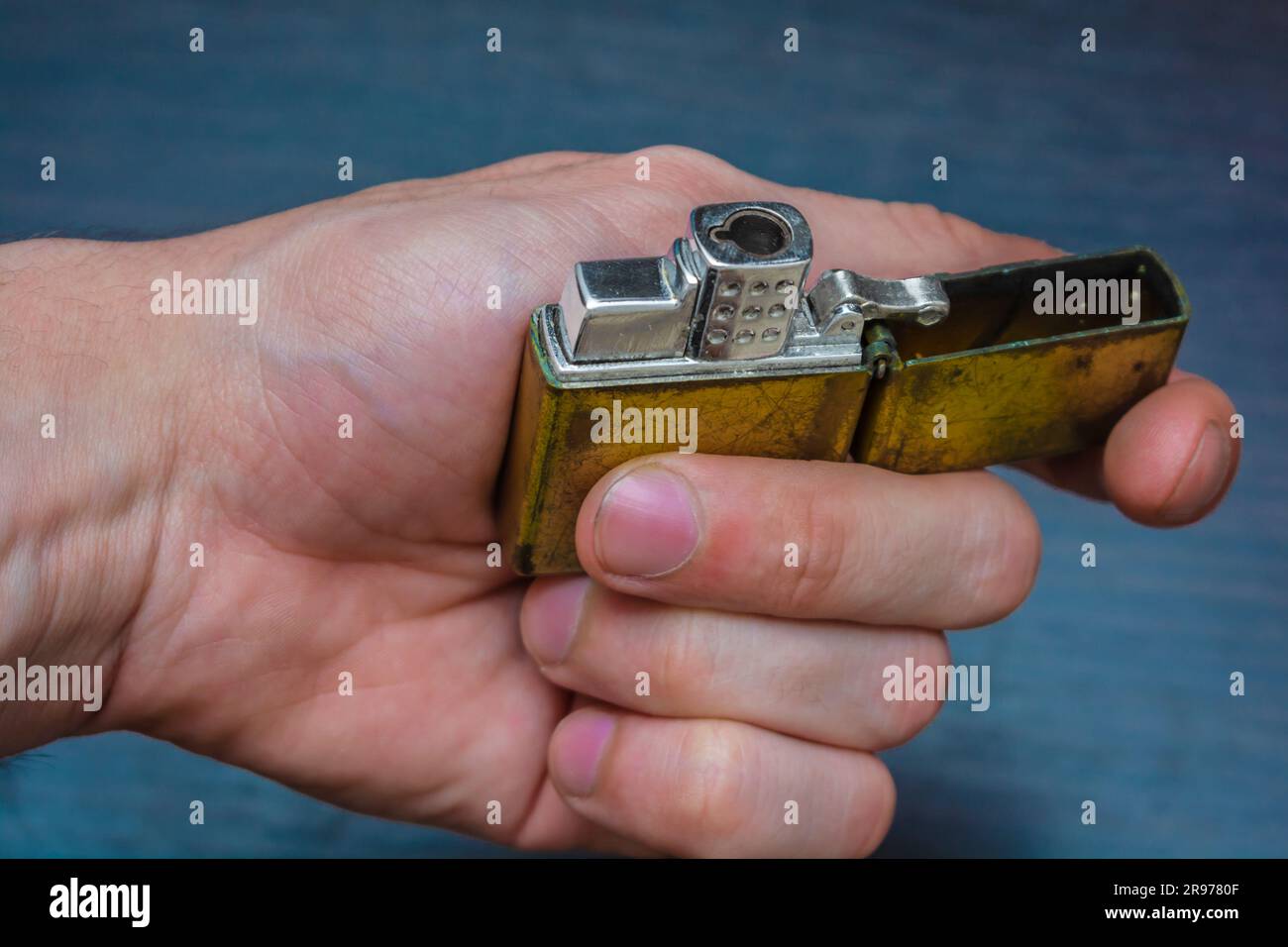 hand-held golden folding lighter on a dark background in yellow-blue ...