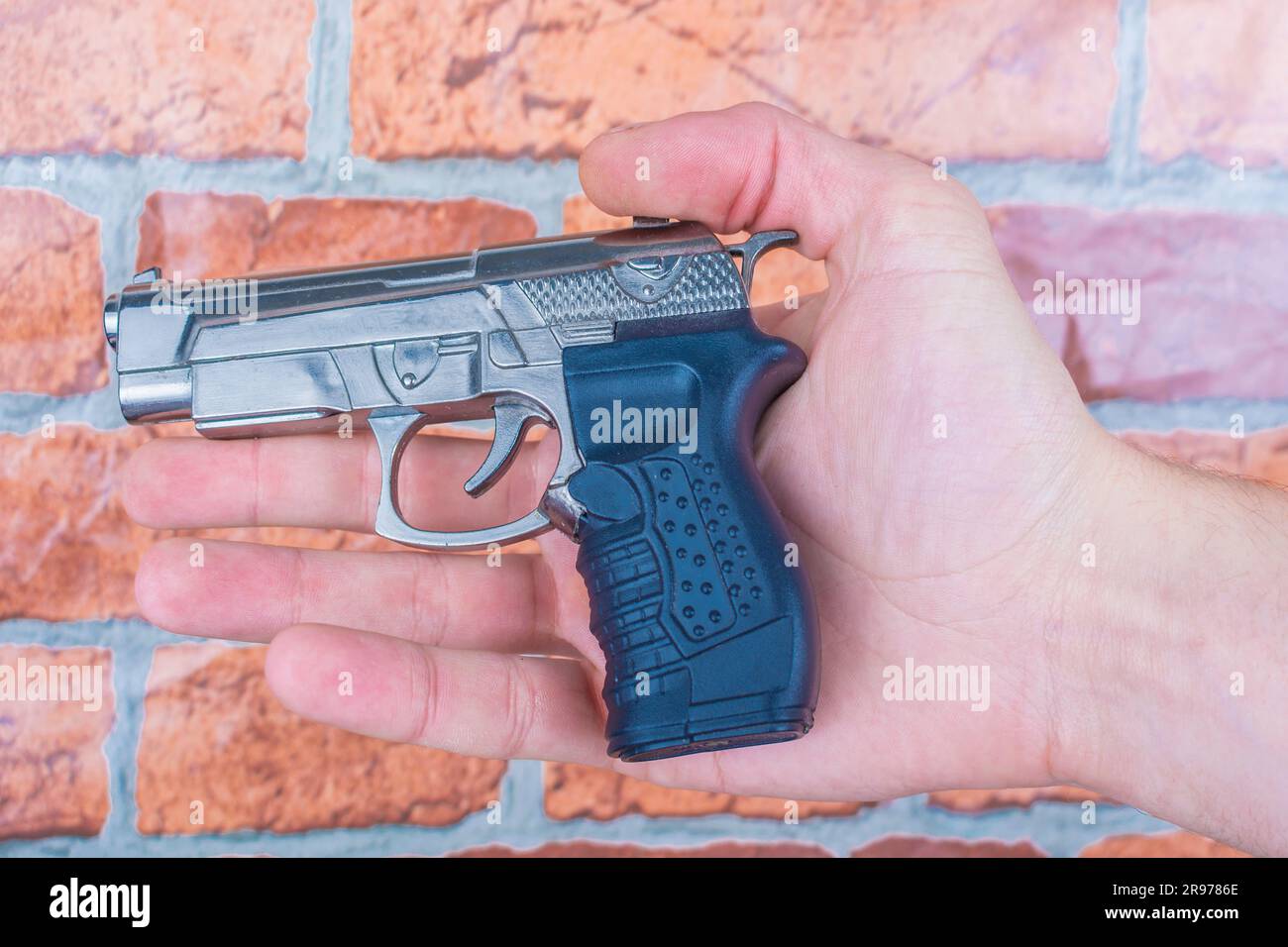 hand of a man with a silver gun on a brick wall background Stock Photo ...
