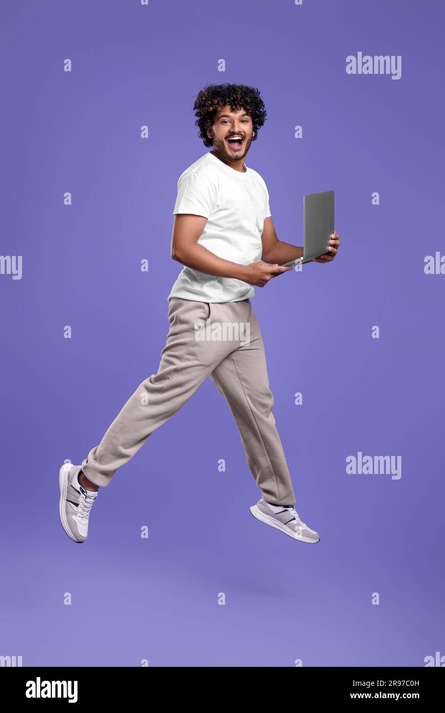 Happy man with laptop jumping on purple background Stock Photo - Alamy