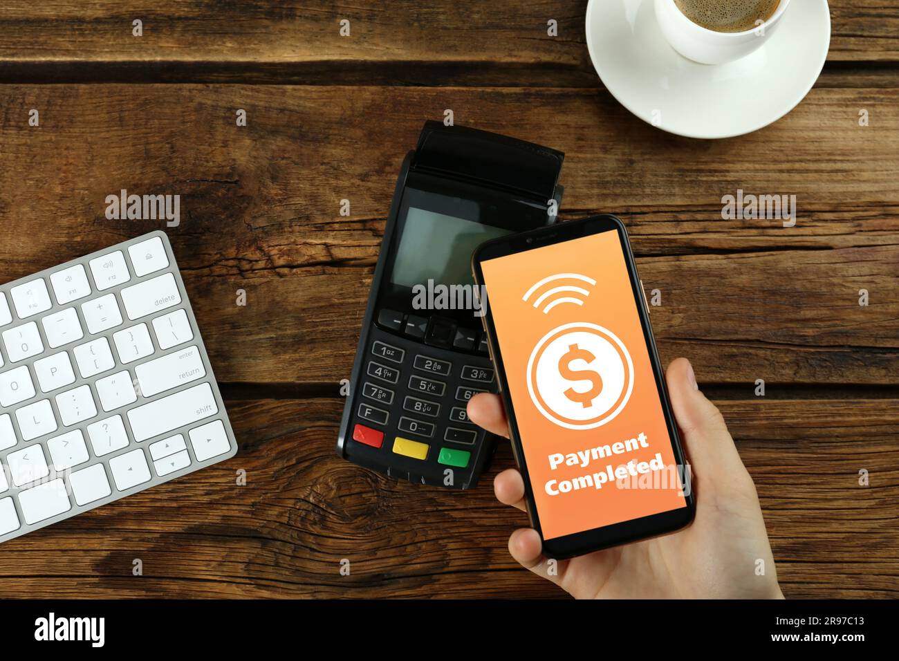 Woman using terminal for contactless payment with smartphone at wooden ...