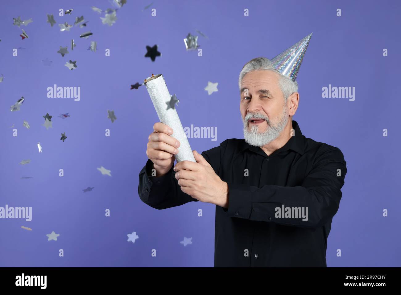 Man blowing up party popper and winking on purple background Stock ...