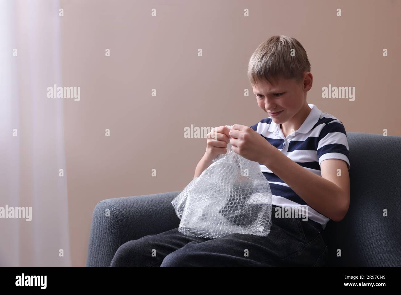 Emotional boy popping bubble wrap indoors. Stress relief Stock Photo ...