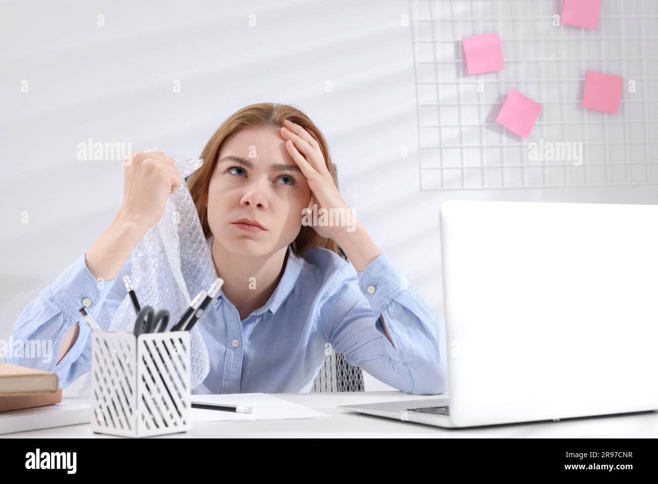Angry woman popping bubble wrap at desk in office. Stress relief Stock ...