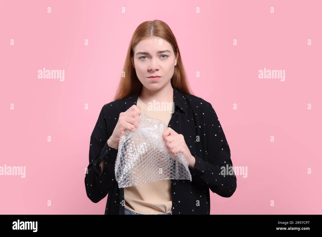 Angry woman popping bubble wrap on pink background. Stress relief Stock ...