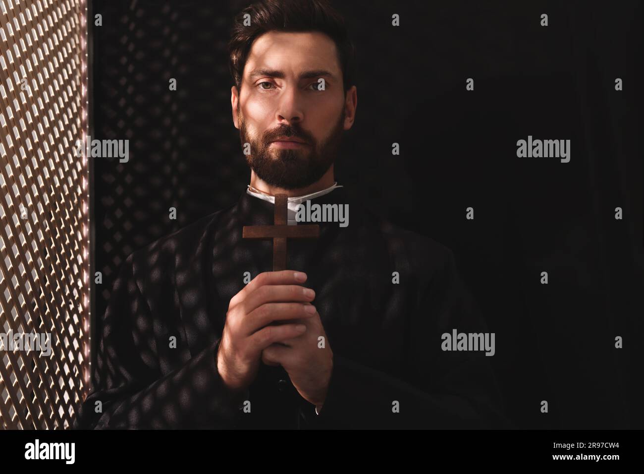Catholic priest in cassock holding cross in confessional Stock Photo ...
