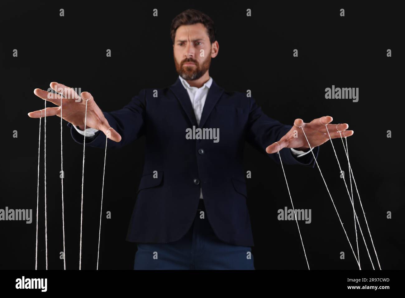 Man in suit pulling strings of puppet on black background, low angle ...