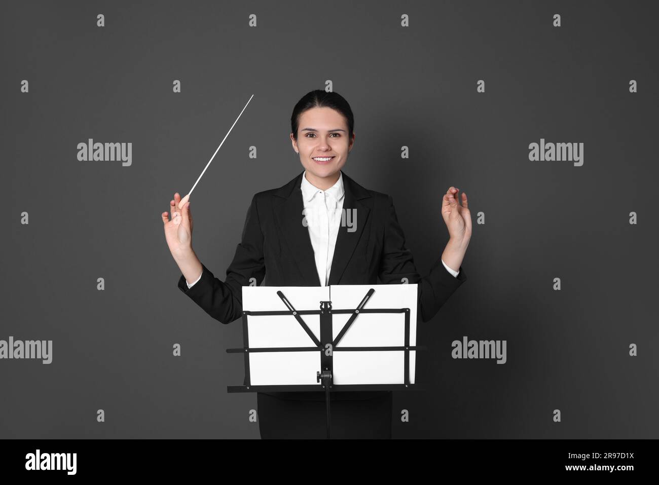 Happy professional conductor with baton and note stand on grey ...