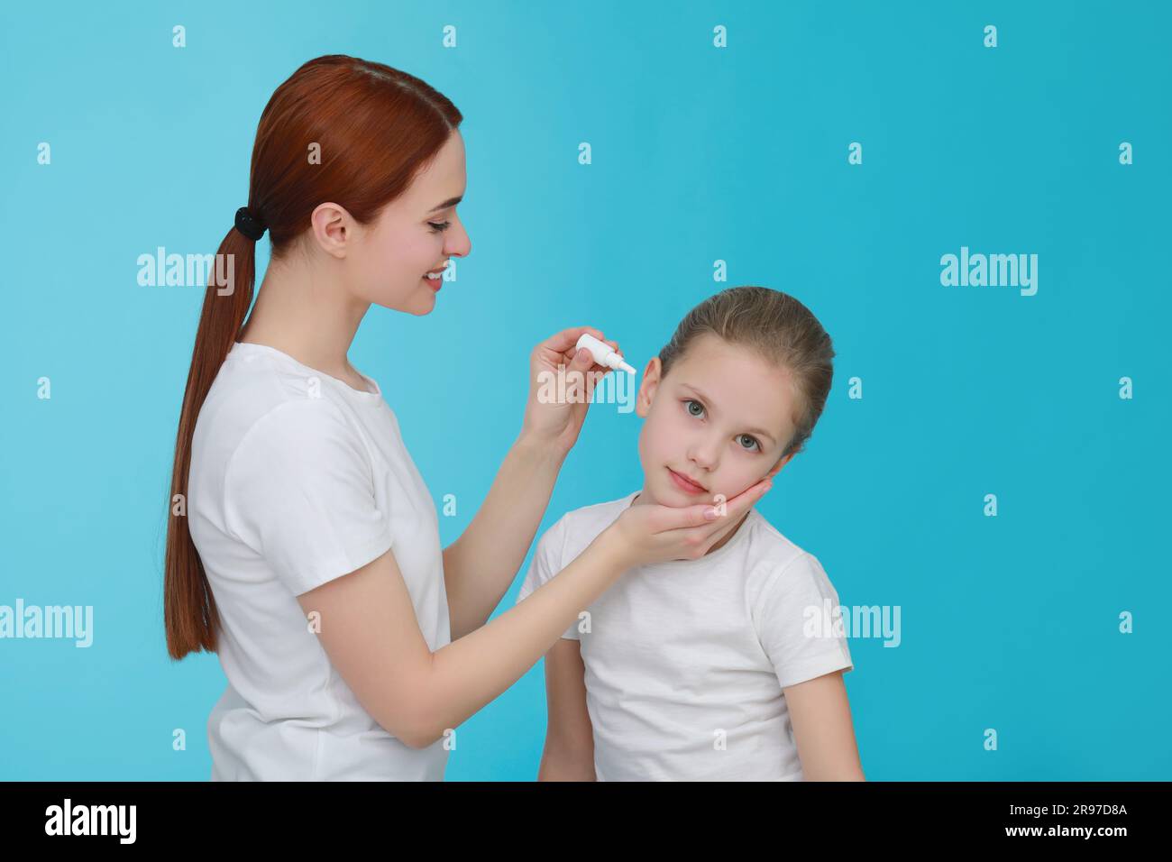 Mother Dripping Medication Into Daughters Ear On Light Blue Background
