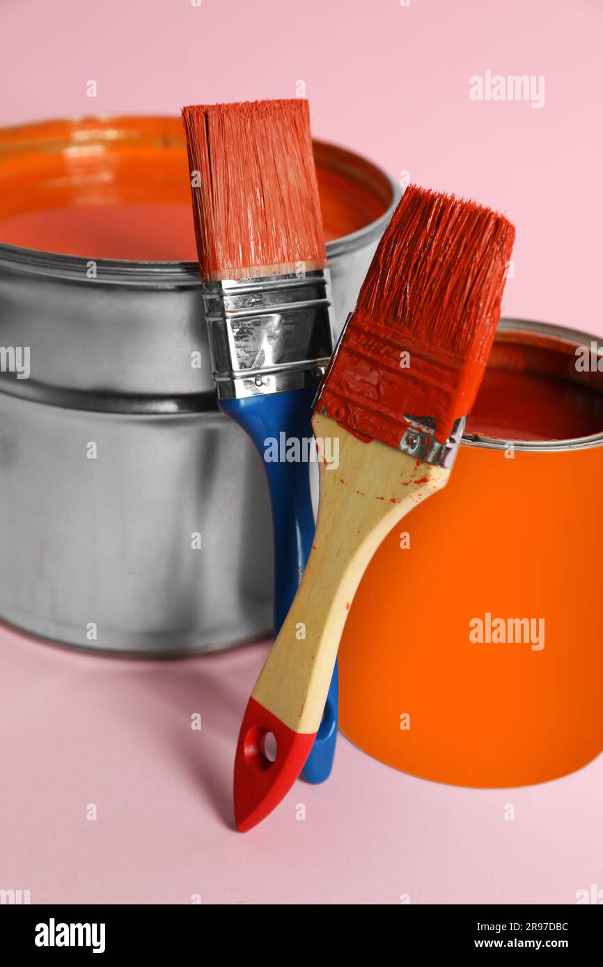 Bucket of orange paint, can and brushes on pink background, closeup ...